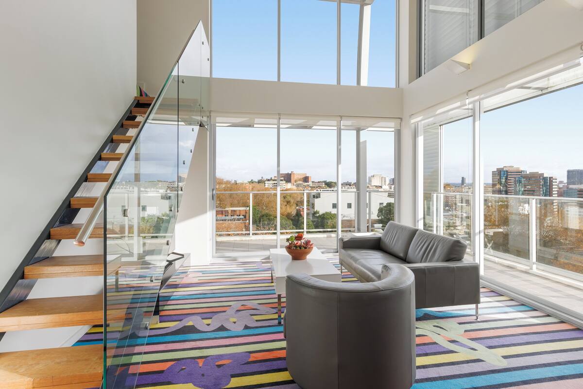 Uma sala de estar moderna com escada, grandes janelas e um tapete colorido listrado.