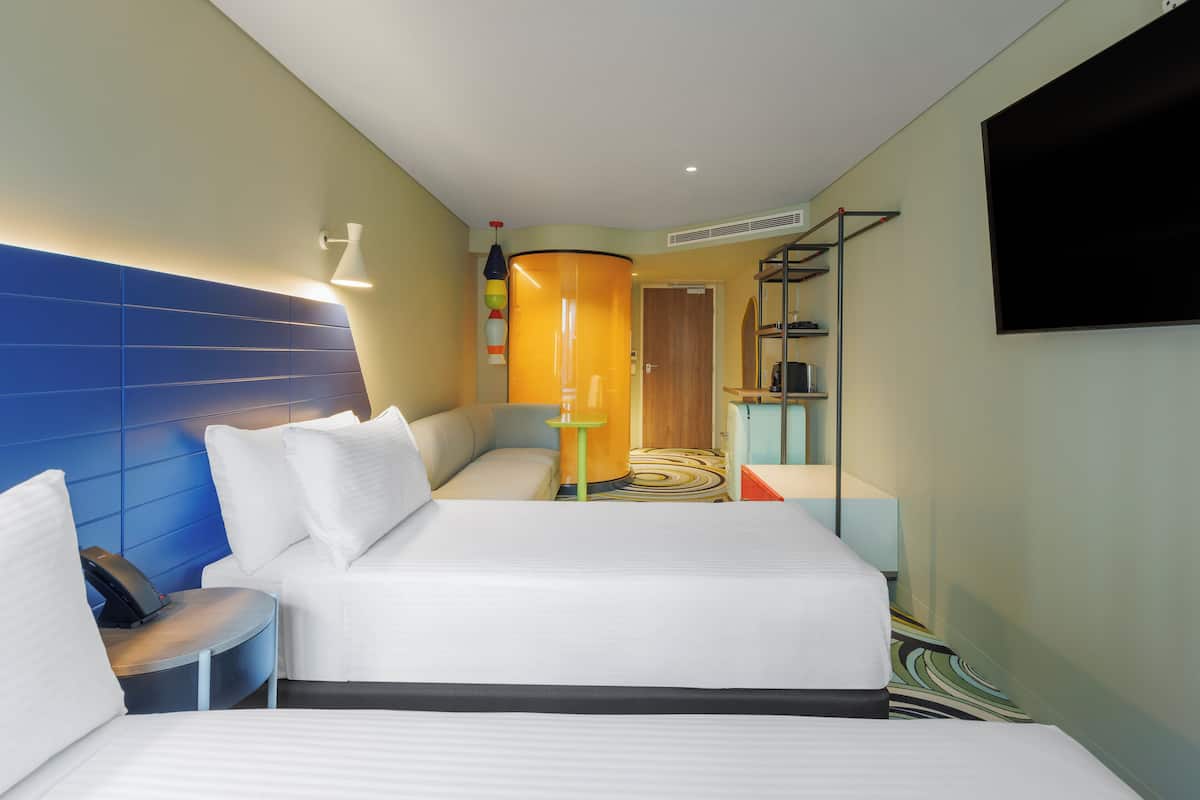 Quarto de hotel com uma cama grande, um sofá, uma mesa pequena, uma TV e um banheiro visível através de uma porta aberta.