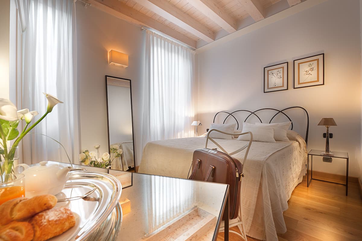 Quarto de hotel com cama, mesas de cabeceira, espelho e bandeja de café da manhã com doces.