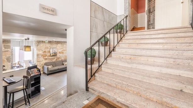 Interior moderno com área de recepção, escada com plantas em vasos e uma parede de pedra.