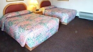 Quarto de hotel com duas camas, cada uma com colcha florida, mesa de cabeceira com abajur e quadros nas paredes.