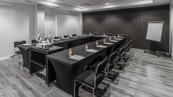 Uma sala de conferência com uma mesa comprida, cadeiras, garrafas de água e bandeiras.