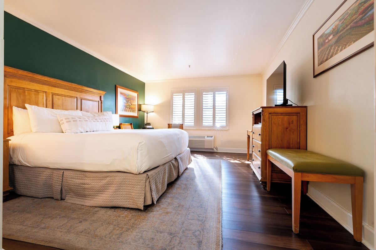 Quarto com uma cama grande, um banco de madeira, cômoda e televisão sobre um suporte.