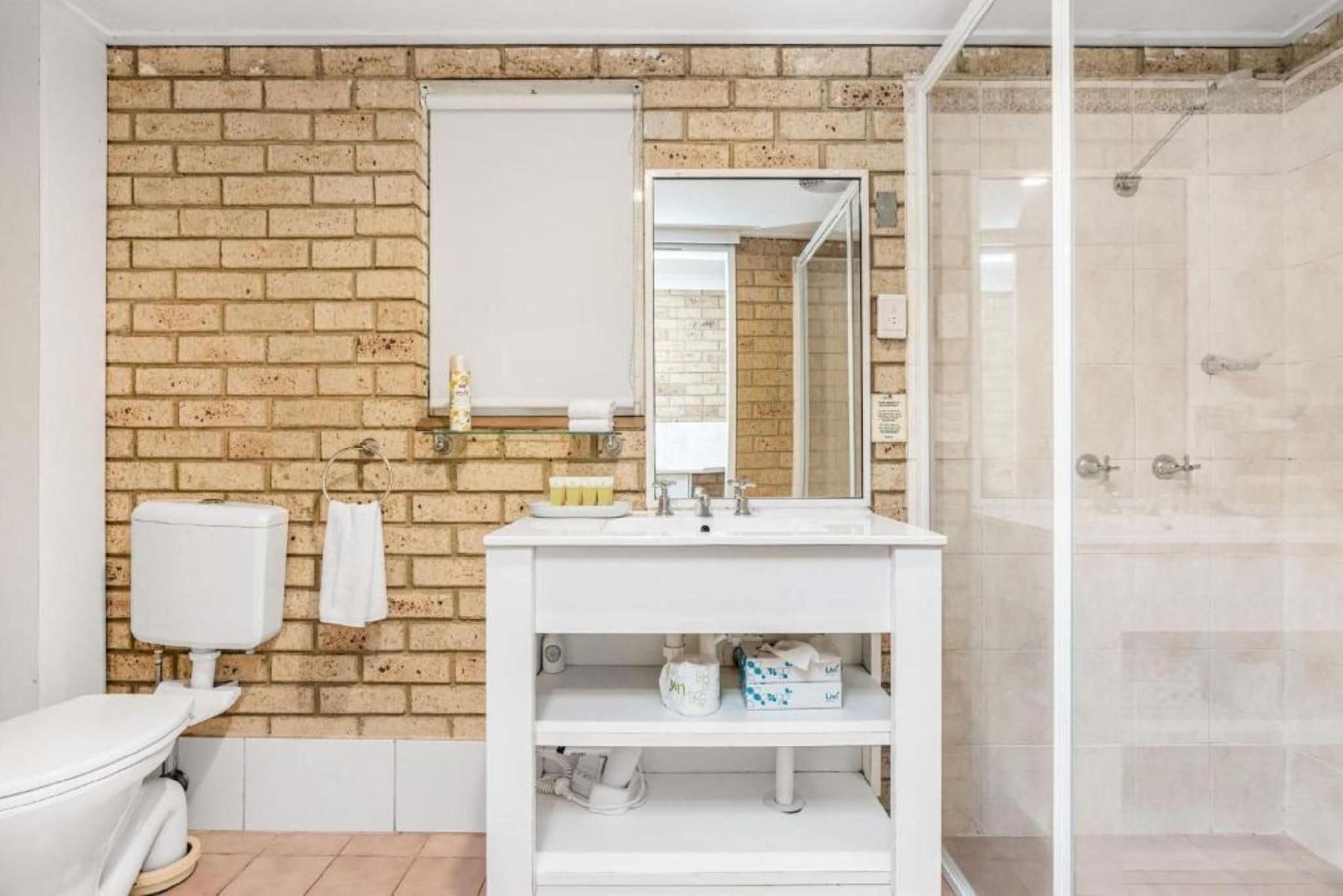 Casa de banho com sanita branca, lavatório com espelho em cima e zona de duche.