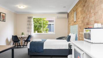Quarto de hotel com cama, escrivaninha, cadeira, micro-ondas e janela com vista para o verde.