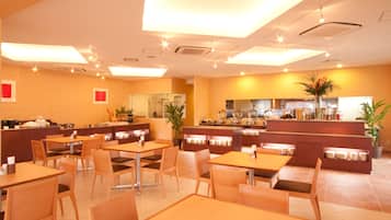 Um restaurante espaçoso com várias mesas e cadeiras, um balcão exibindo diversos alimentos e uma área de cozinha ao fundo.