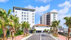 Um hotel com entrada central, rodeado por palmeiras e um céu claro.