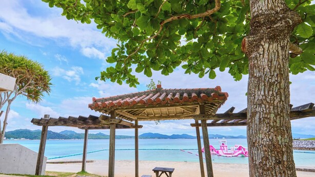 Um pavilhão à beira-mar com telhado em azulejos, parede de concreto e vista para o mar.