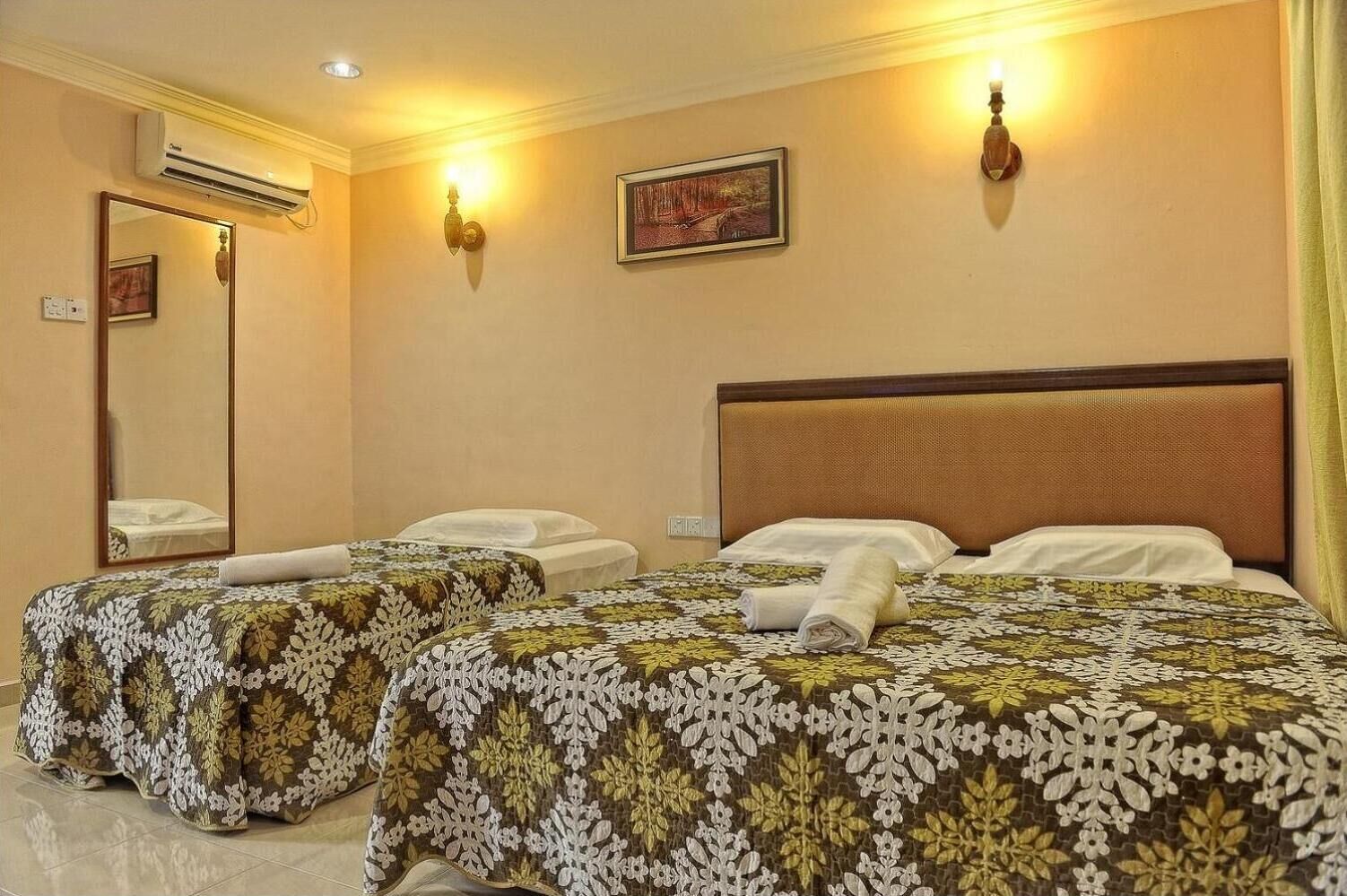 Quarto de hotel com duas camas, cada uma com roupa de cama estampada em florais, um espelho grande e iluminação fixada na parede.