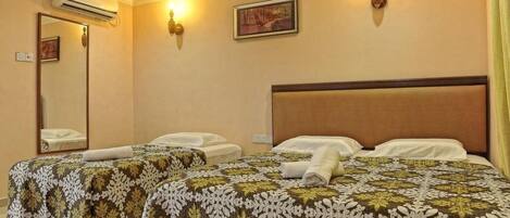 Quarto de hotel com duas camas, cada uma com roupa de cama estampada em florais, um espelho grande e iluminação fixada na parede.