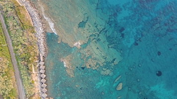 Vista aérea de uma área costeira com falésias rochosas, uma linha férrea e águas azul-claras.