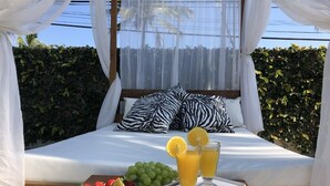 Cama com dossel, almofadas com padrão de zebra e bandeja com frutas e copos de suco.