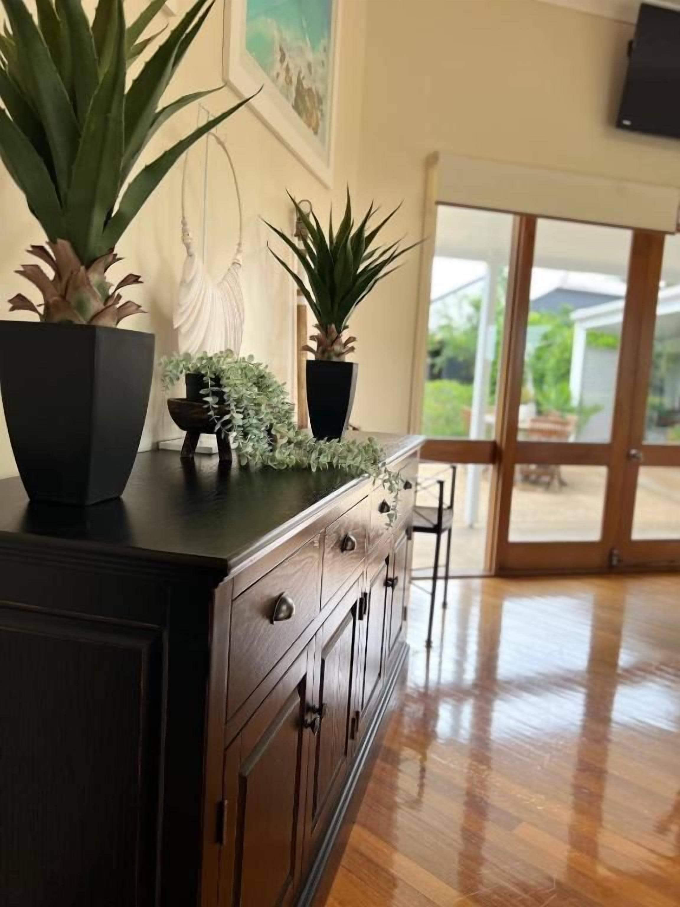 Quarto com piso de madeira, um armário escuro com plantas e uma porta de vidro deslizante que dá para uma área externa.