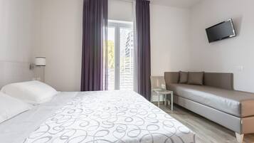 Quarto de hotel com cama, sofá, televisão e janela com cortinas.