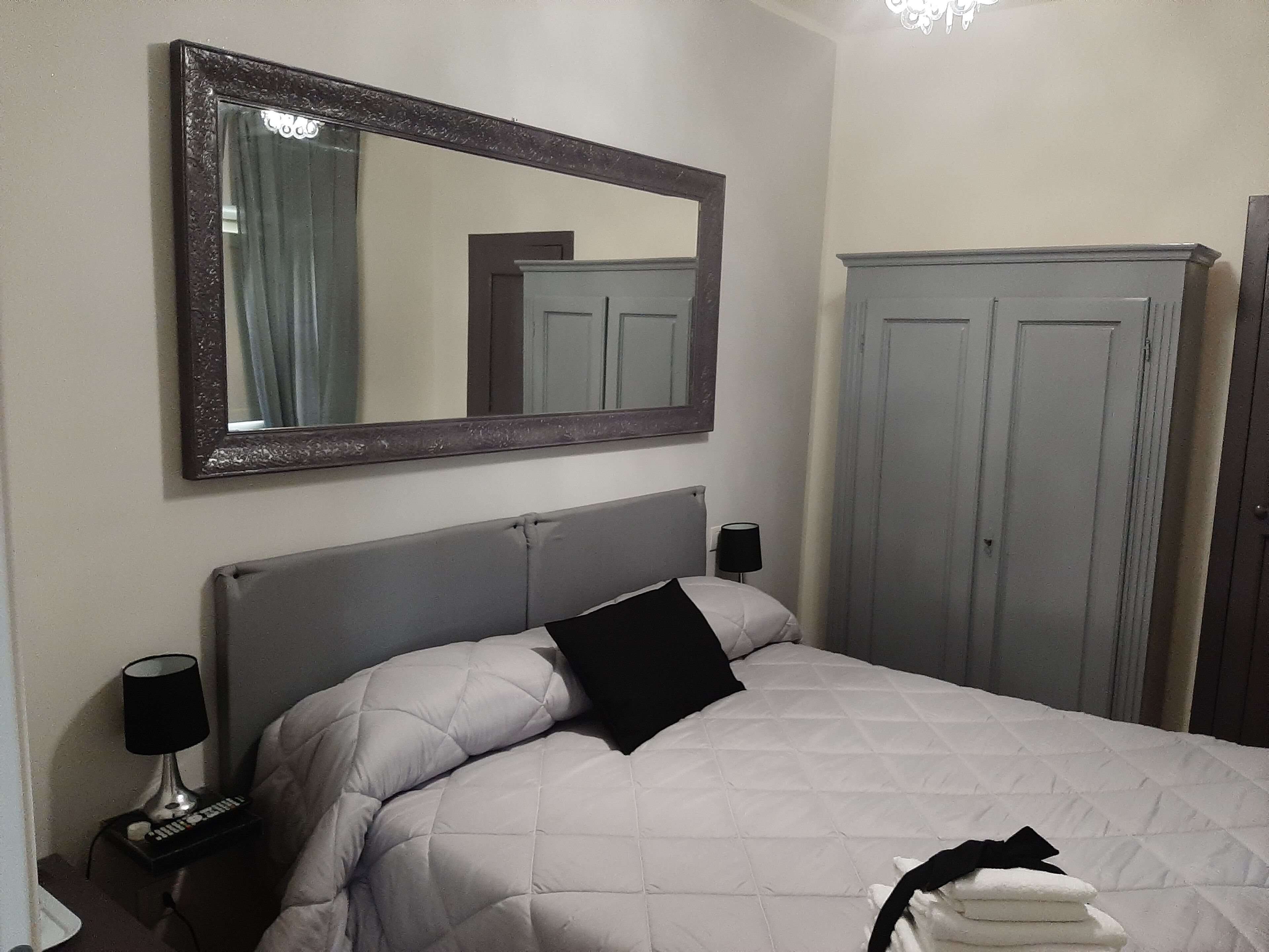 Quarto com cama, espelho grande, armário e mesa de cabeceira com abajur.