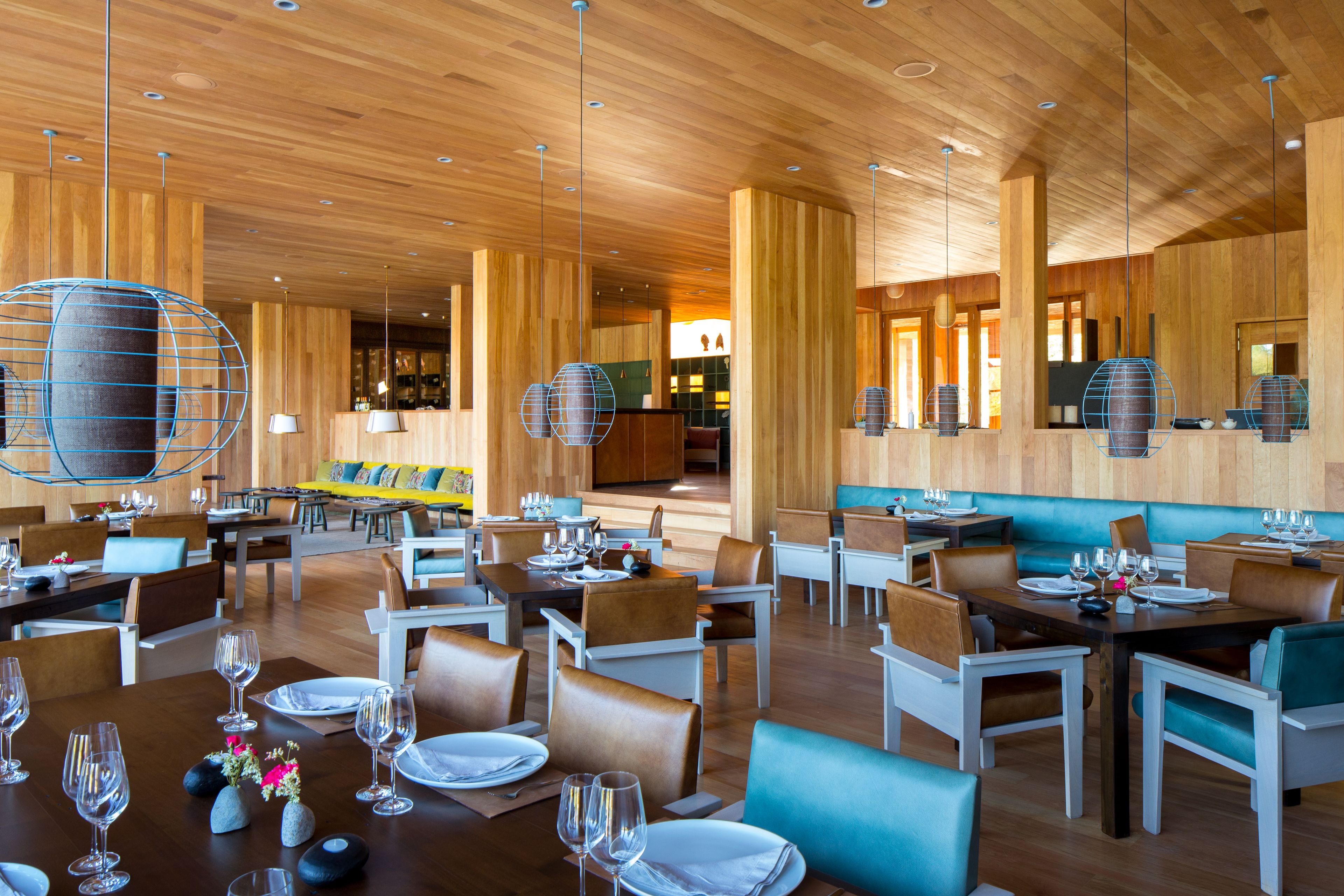 Restaurante moderno com paredes revestidas de madeira, várias mesas de jantar e assentos acolchoados azuis.