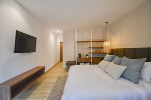 Um quarto moderno com uma cama grande, uma televisão presa à parede e um banco de madeira.