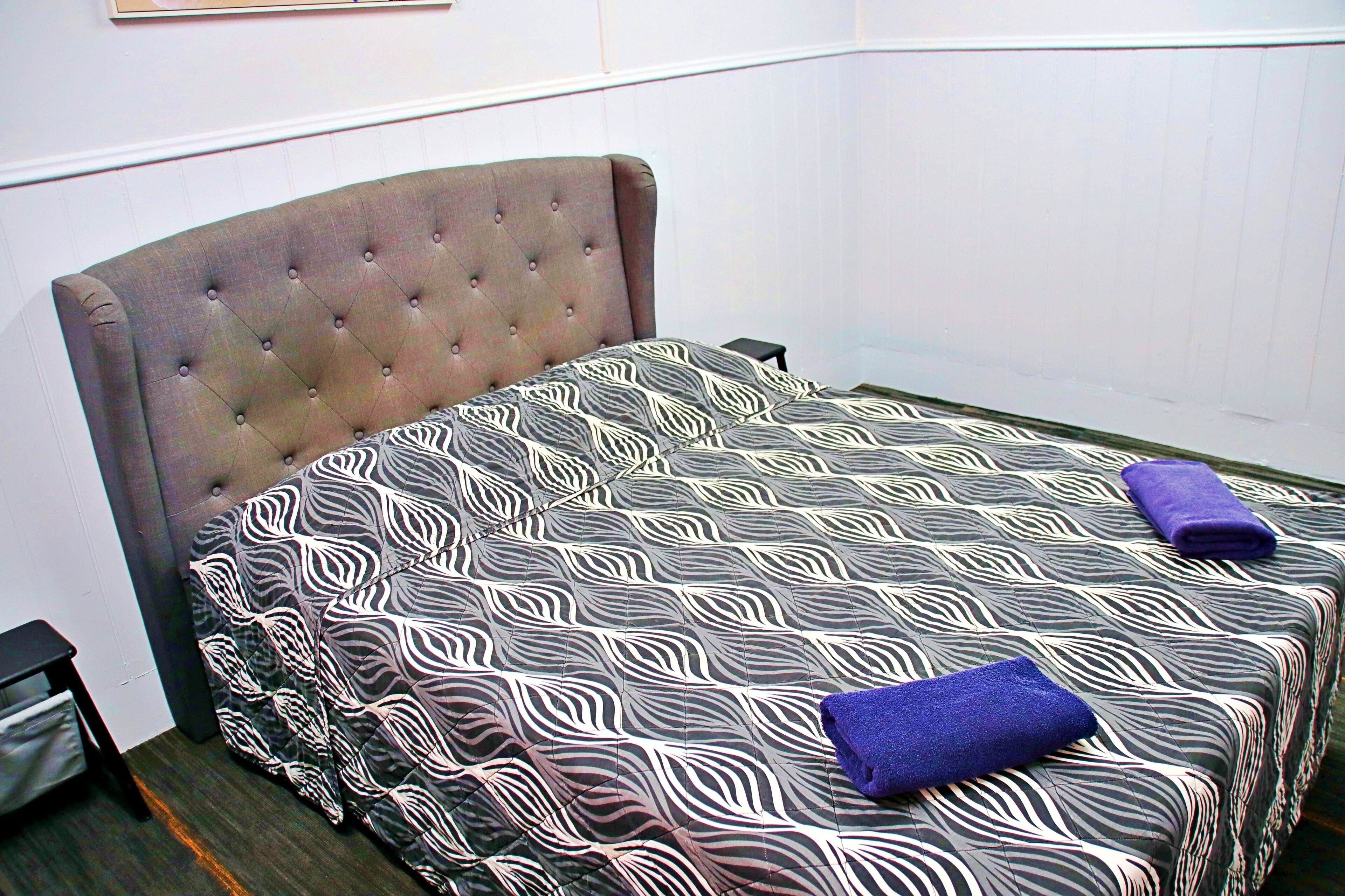 Uma cama com cabeceira estofada, espalha roupa de cama estampada e duas toalhas dobradas.
