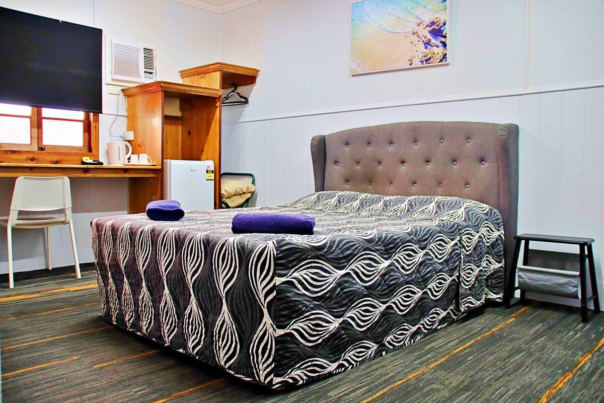 Um quarto com uma cama grande, uma escrivaninha com um computador, uma cadeira e uma pequena mesa.