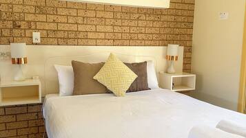 Quarto de hotel com parede em padrão tijolo, cama com roupa de cama branca, duas luminárias de cabeceira e um aparelho de ar condicionado.