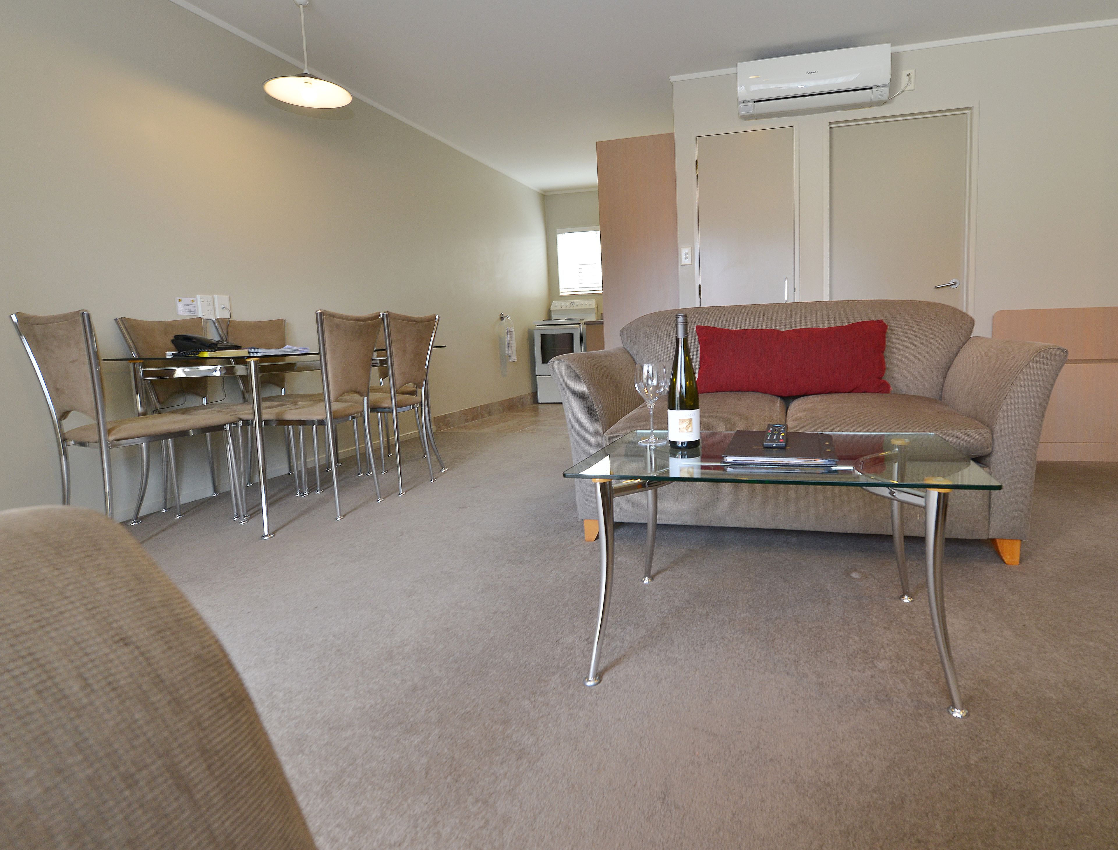Uma sala de estar com uma mesa de centro de vidro, um sofá com almofada vermelha e uma área de jantar com cadeiras e mesa.