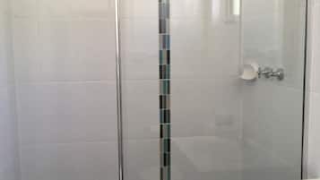 Um banheiro moderno com box de vidro, pia branca e paredes revestidas de azulejo.
