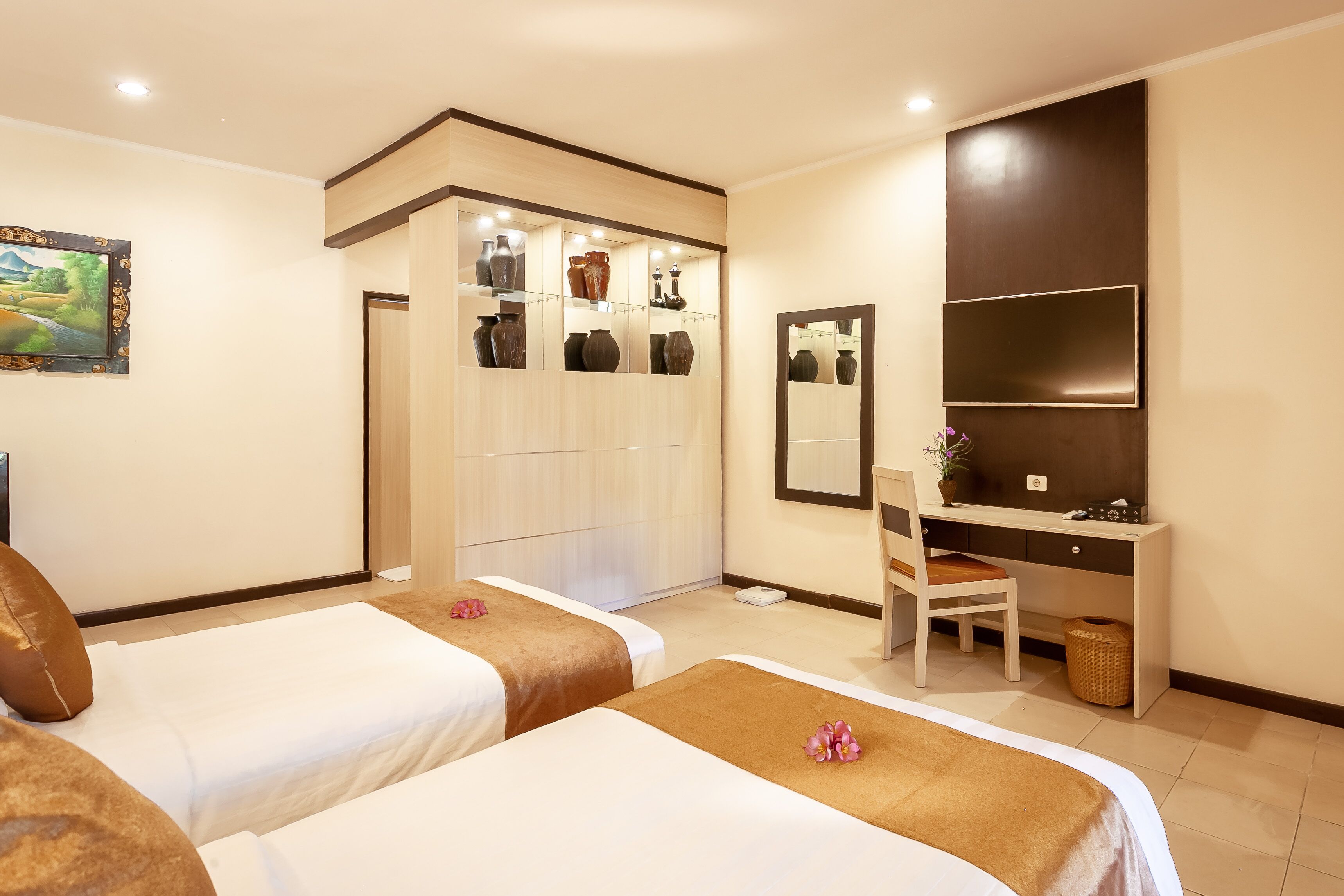 Quarto de hotel com duas camas, uma escrivaninha, um espelho e uma estante com objetos decorativos.
