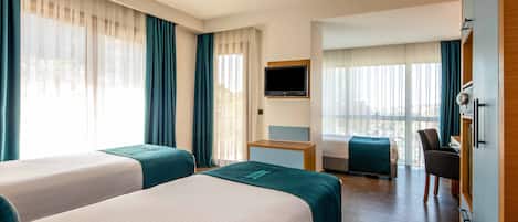 Quarto de hotel com duas camas, televisão, escrivaninha e vista para a cidade.