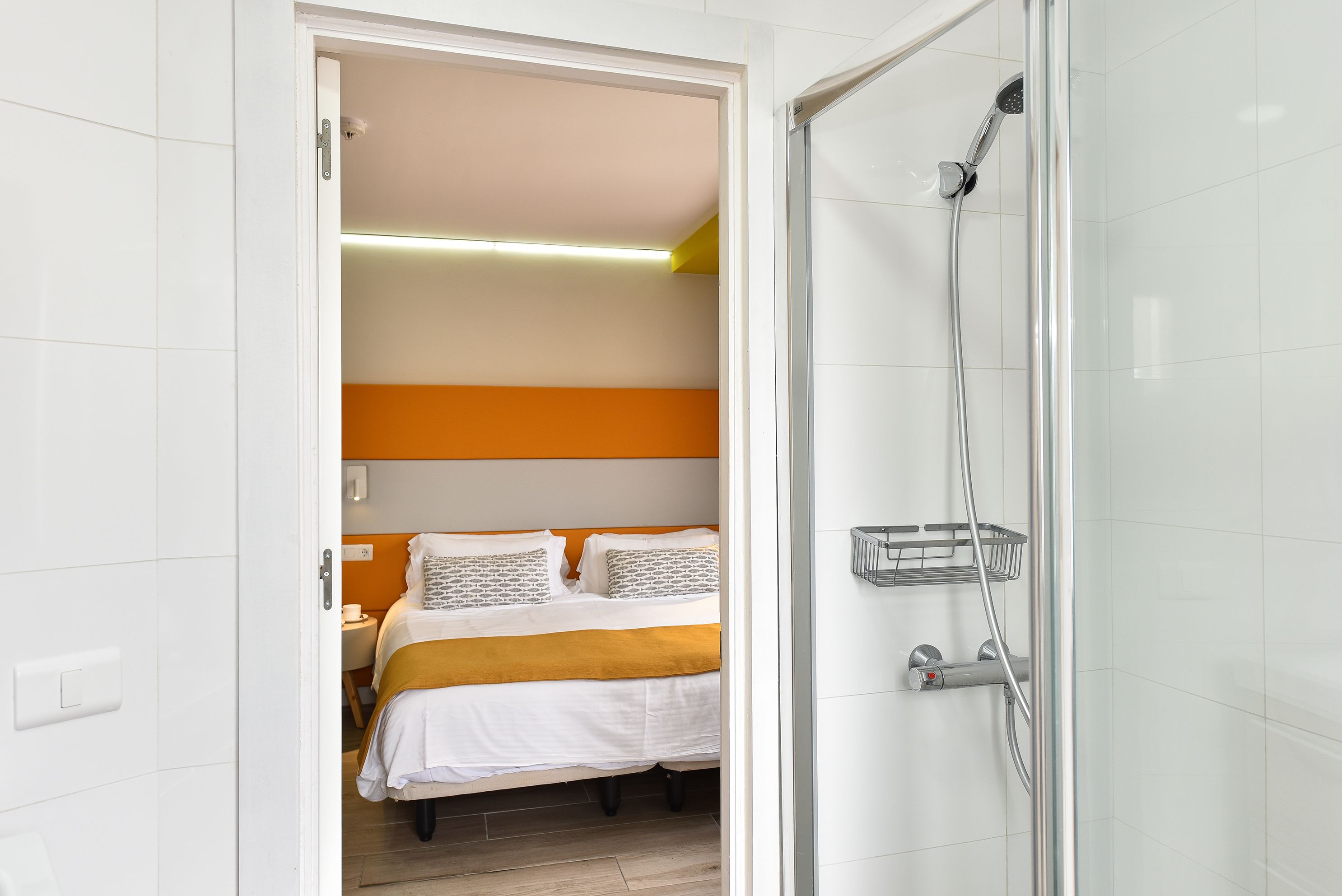 Quarto de hotel com cama, mesa de cabeceira e área de chuveiro.