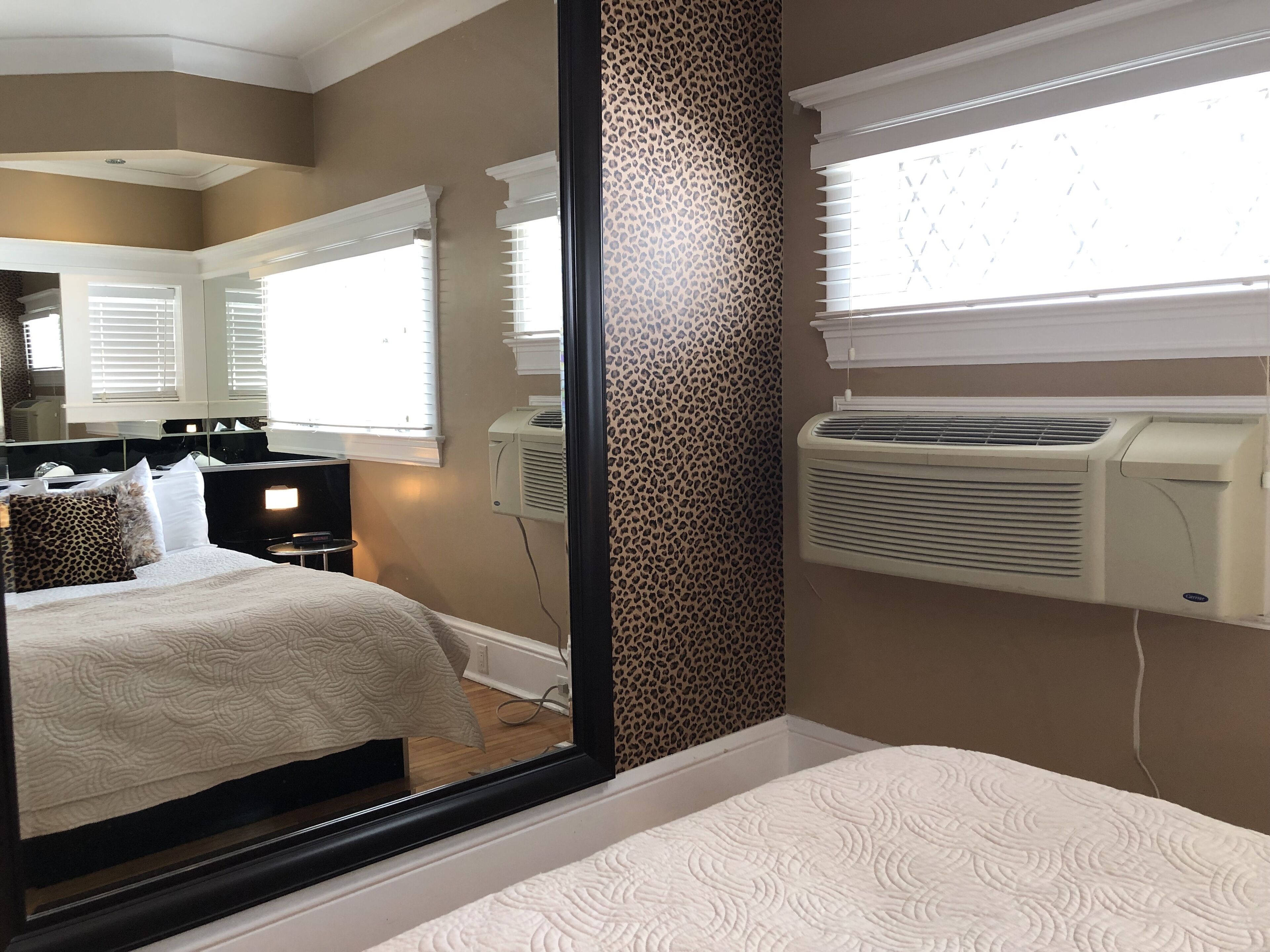 Quarto com cama grande, espelho, janela com persianas, ar condicionado e parede com estampa de leopardo.
