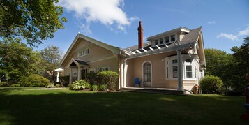 Uma casa de dois andares com varanda frontal, chaminé e gramado bem cuidado.