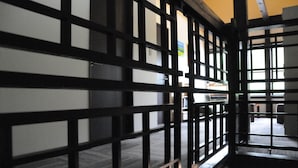 Um quarto com porta tradicional japonesa estilo shoji, piso de madeira e vista para um corredor com um banco e uma mesa.