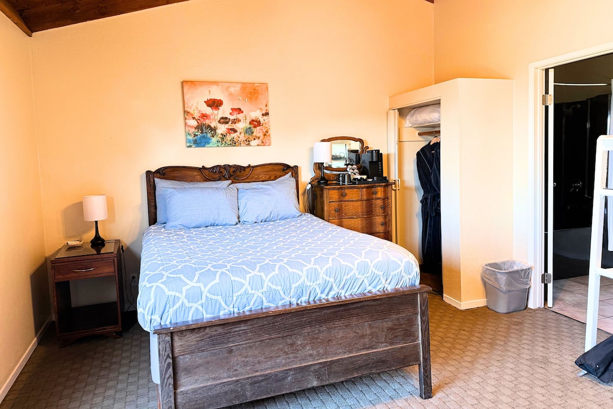 Quarto com cama de madeira, mesa de cabeceira, cômoda, quadro e armário.