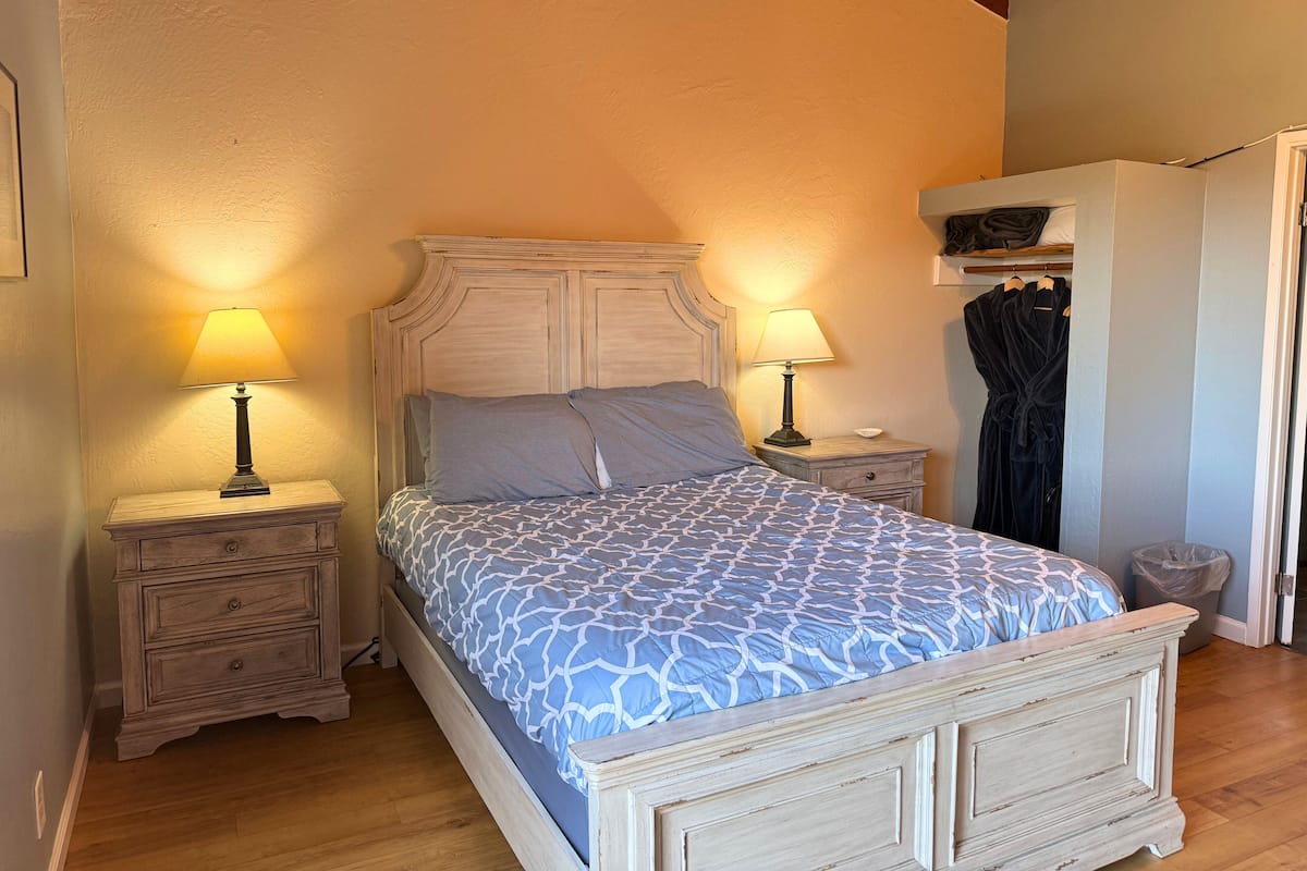 Quarto com cama, duas mesas de cabeceira, um criado-mudo, cômoda de madeira e roupão pendurado em um cabide.