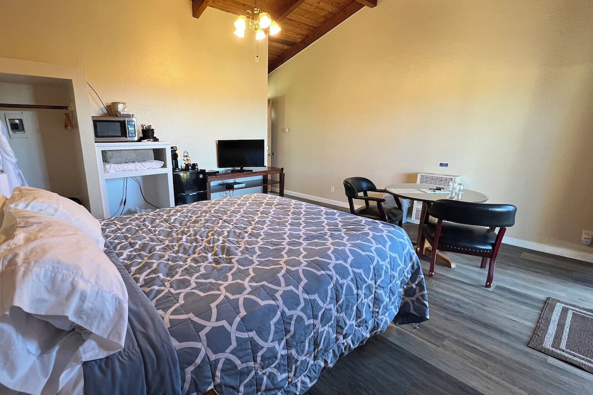 Quarto de hotel com uma cama, uma escrivaninha com computador, uma televisão e uma cadeira.
