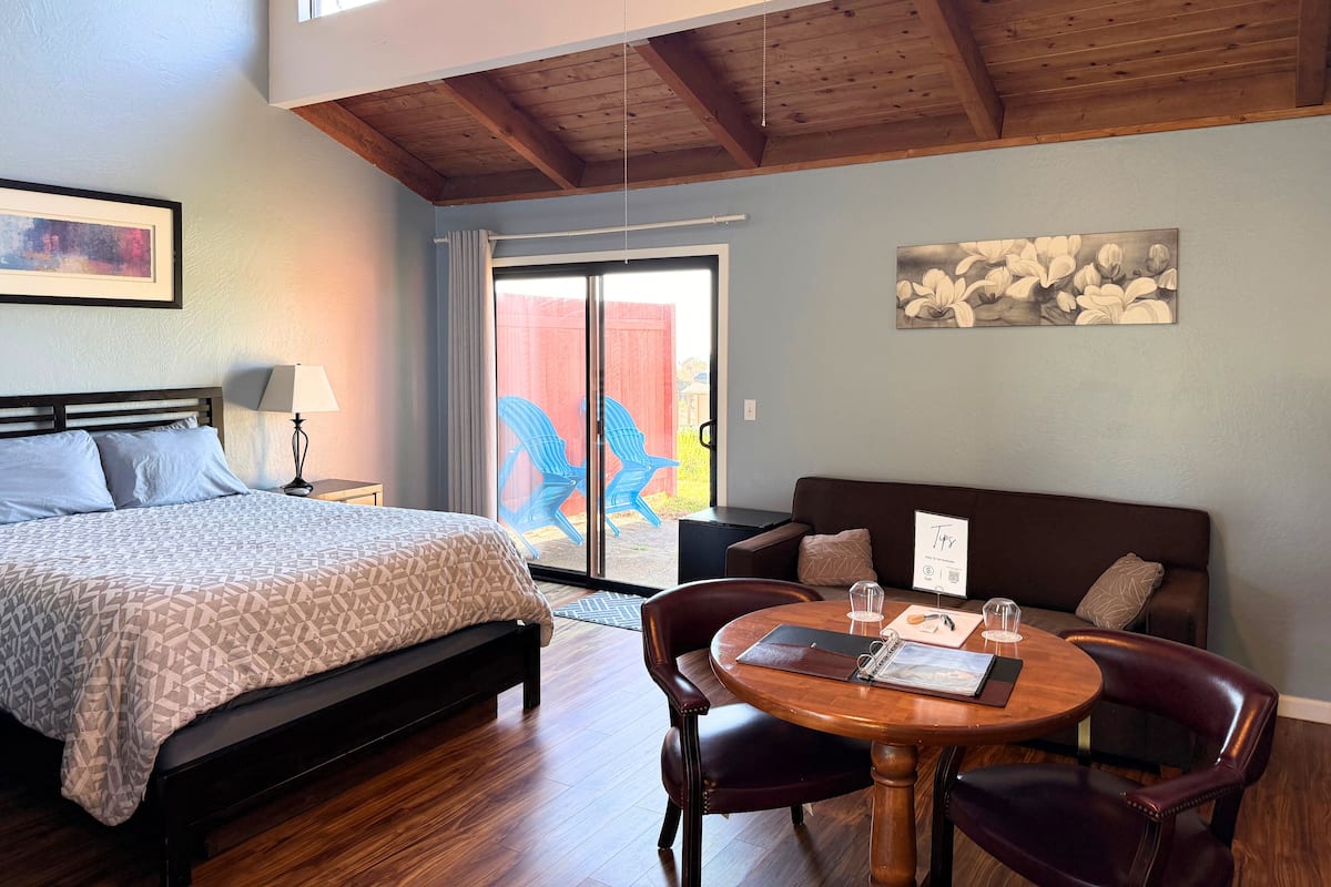 Um quarto com cama, mesa de cabeceira, abajur, sofá, mesa de jantar com cadeiras e uma porta de vidro deslizante para um pátio.