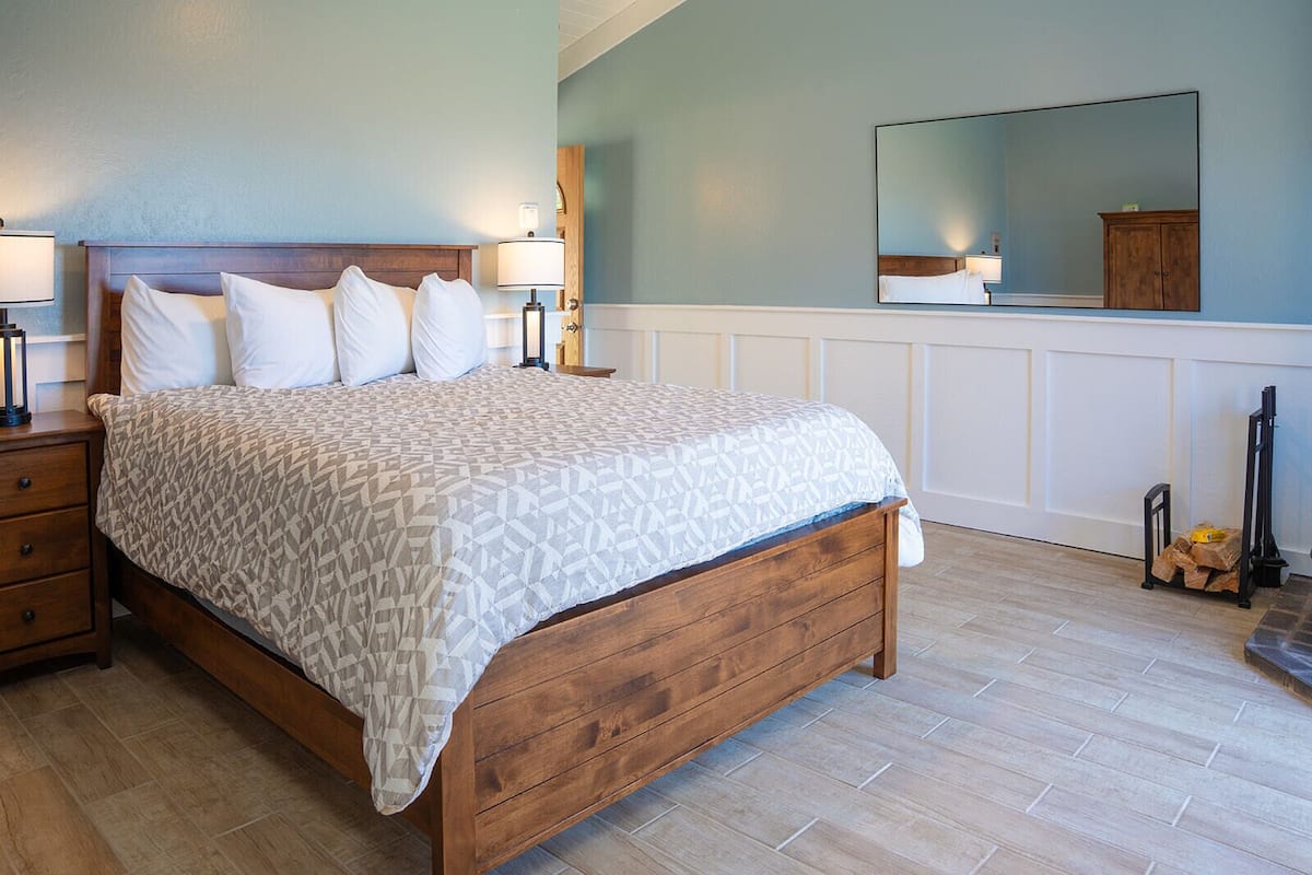 Cama bem arrumada com colcha estampada, cabeceira de madeira e duas luminárias de cabeceira.