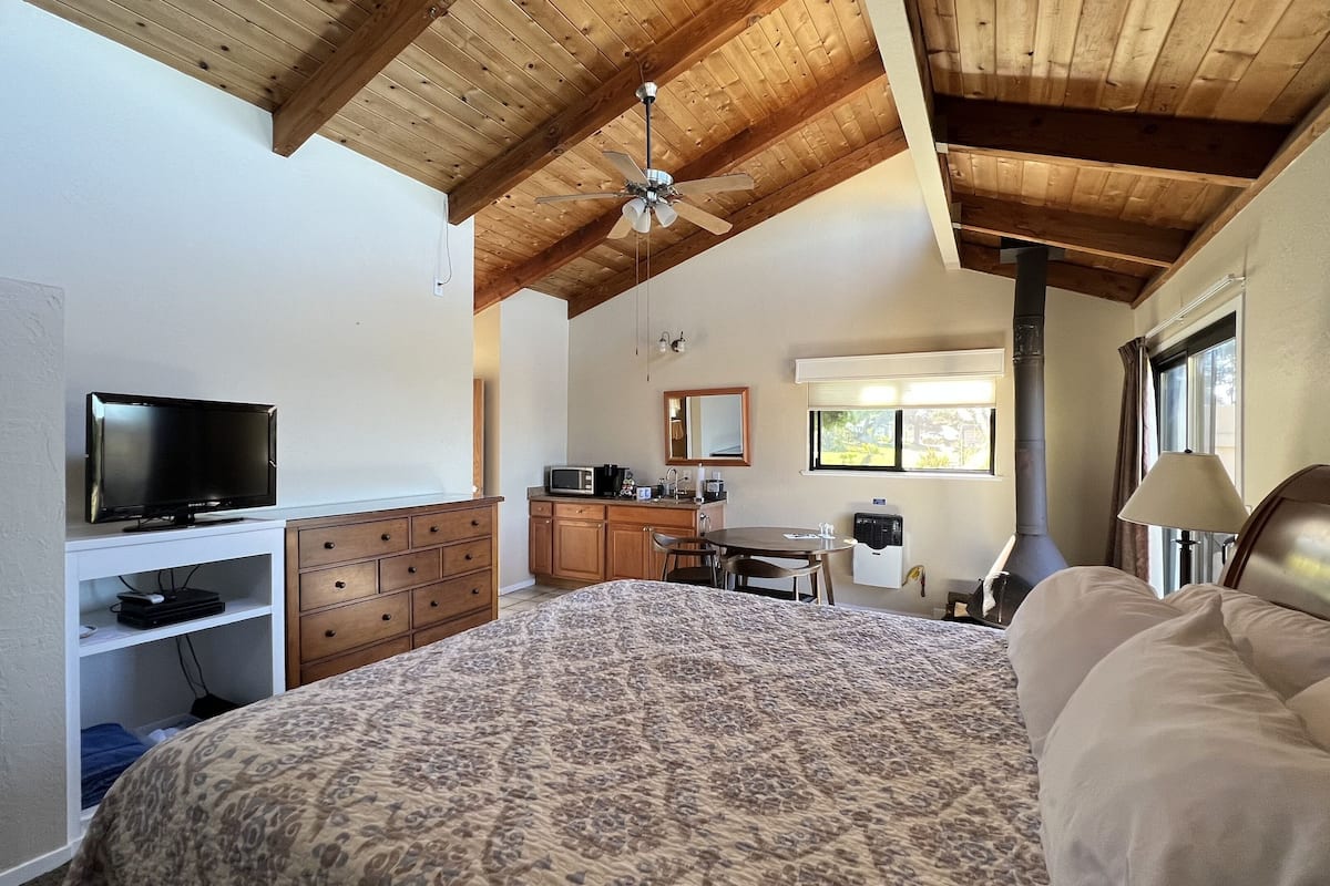 Quarto com cama grande, vigas de madeira no teto, televisão, cozinha compacta e janela com vista.