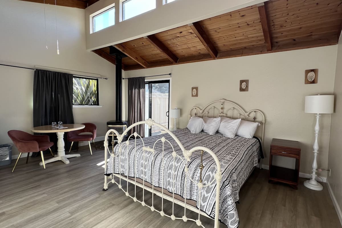 Quarto com cama, mesa de cabeceira, abajur, cadeira, mesa e janela.