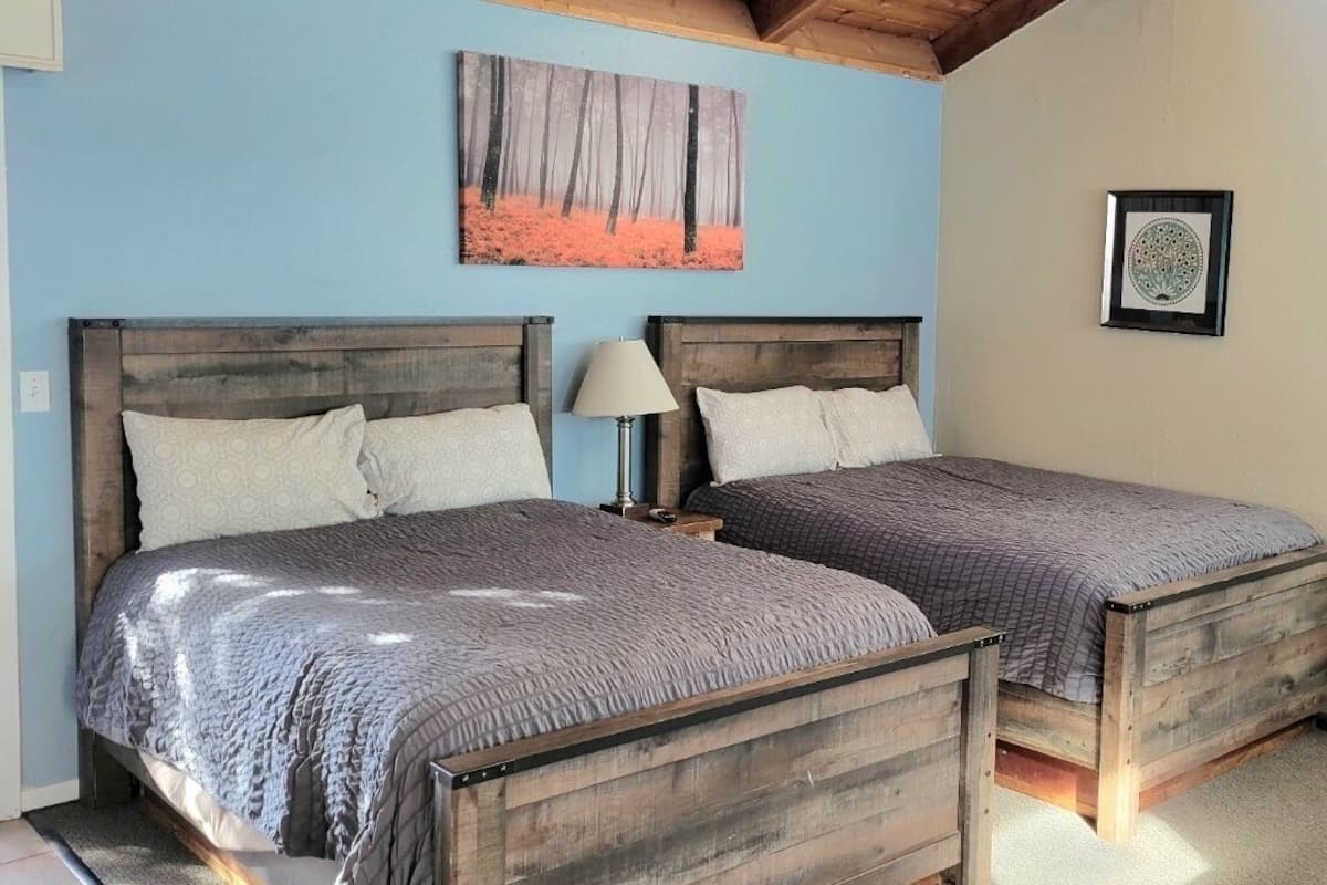 Quarto com duas camas de madeira, teto com vigas aparentes e um quadro na parede.