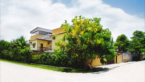 Uma casa moderna de dois andares com varanda, rodeada por vegetação exuberante e um céu limpo.