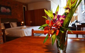 Quarto de hotel com cama, cabeceira de madeira e um vaso de flores sobre uma mesa.