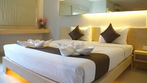 Cama bem arrumada com lençóis brancos e almofadas decorativas, mesa de cabeceira com abajur e um espelho grande sobre a cama.