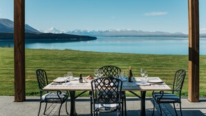Uma área de refeições ao ar livre com uma mesa posta para dois, com vista para um lago e montanhas.