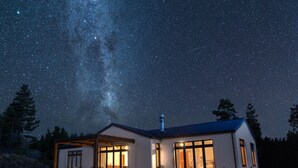 Uma casa com uma grande porta de vidro, uma chaminé e um céu noturno estrelado.