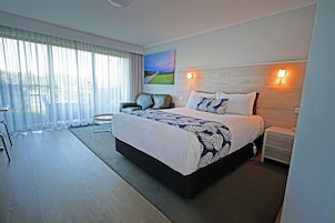 Um quarto moderno com uma cama grande, uma cadeira, uma mesinha e um quadro na parede.