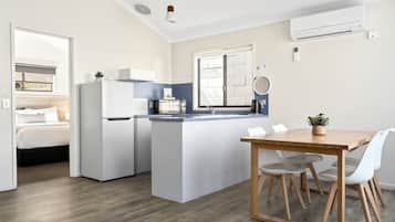 Cozinha compacta com ilha central, área de refeições com mesa e cadeiras de madeira, e uma janela visível.