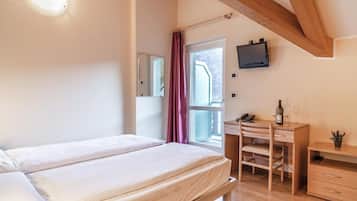 Quarto com cama, escrivaninha, cadeira, televisão e janela com cortinas.