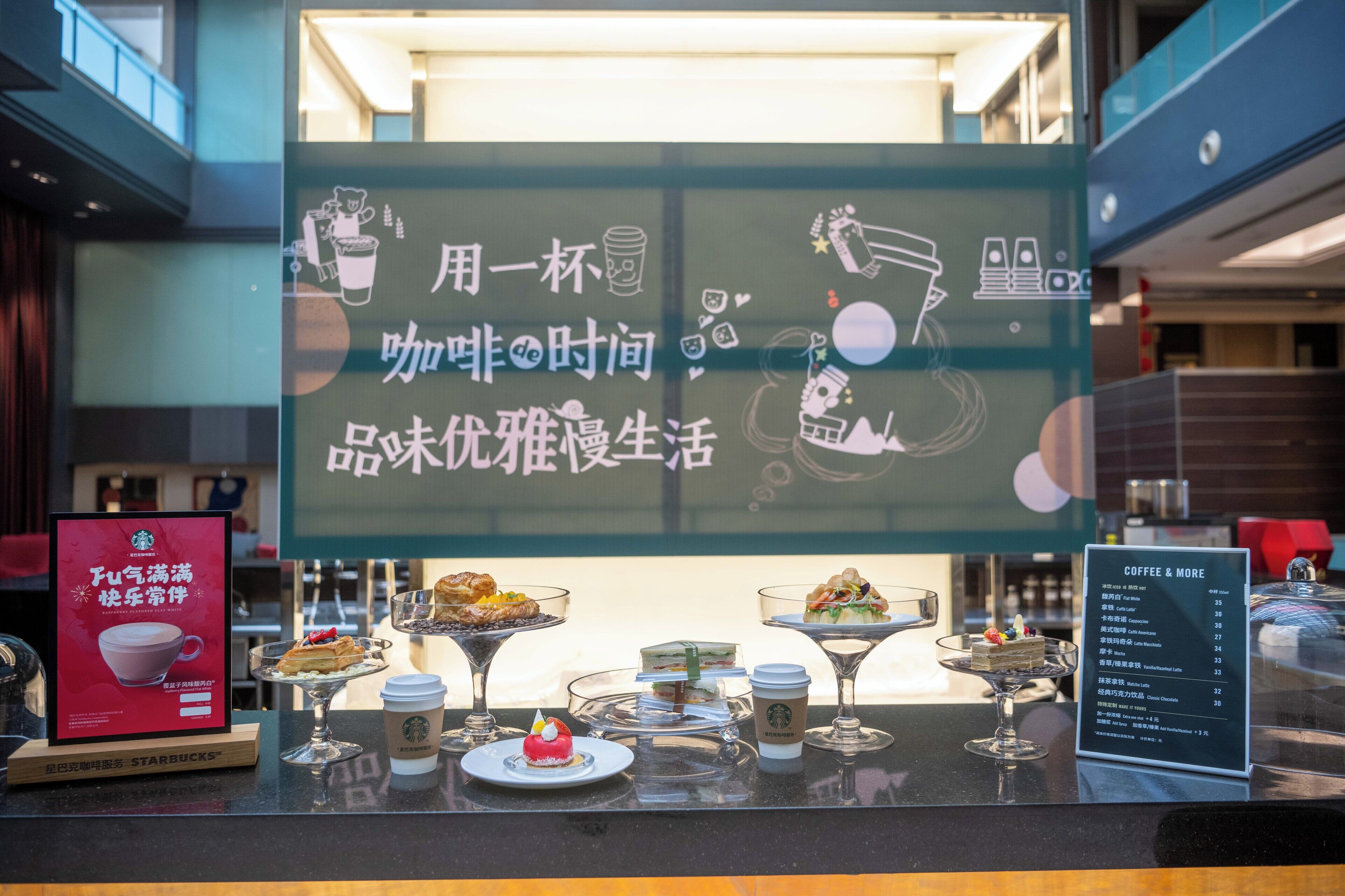 Um balcão da Starbucks com um quadro de menu, diversos doces e xícaras de café.