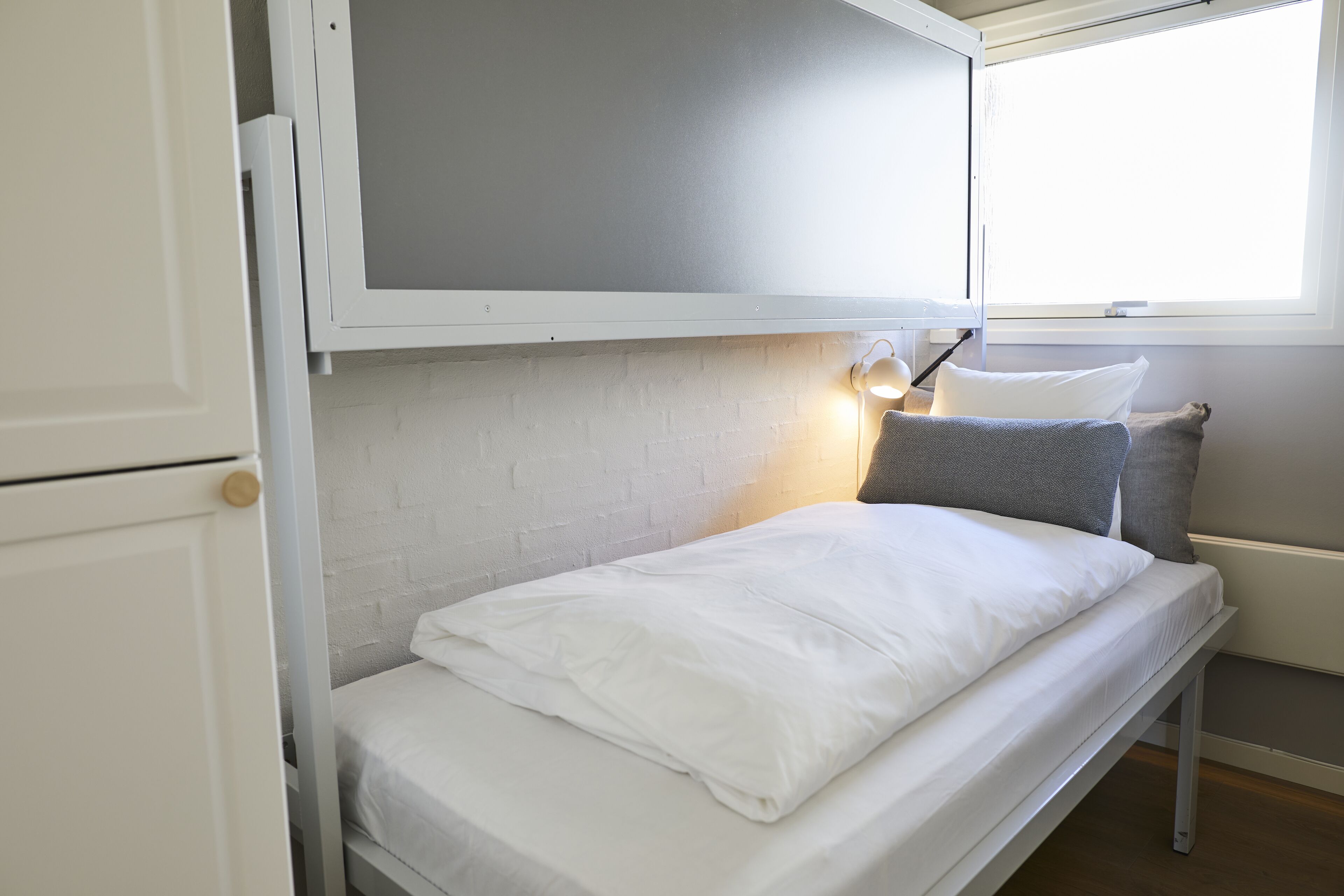 Quarto pequeno com uma cama de solteiro, dossel branco e janela com luz natural.